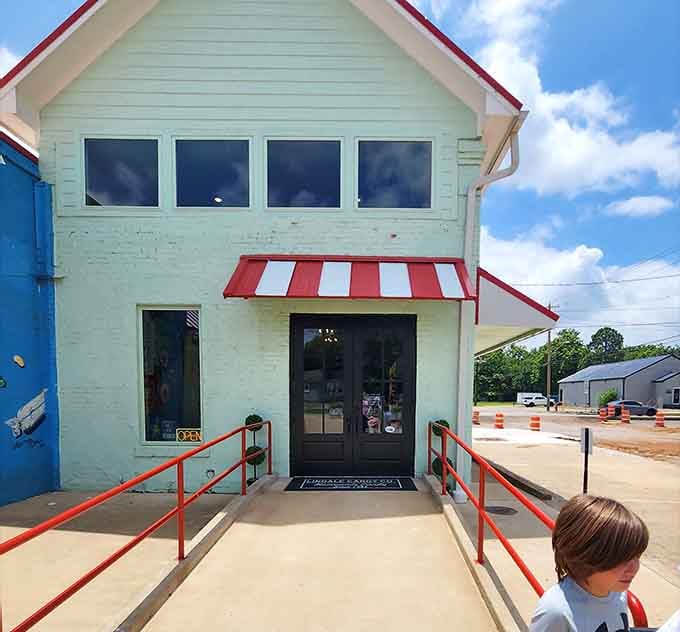 A mint green building with red trim that says, "Come in, happiness is mandatory here."