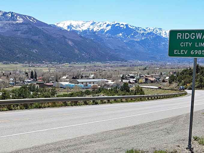 The Ridgway city limits sign at 6,985 feet elevation, where the mountains announce themselves immediately and dramatically.