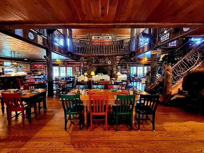 Log walls, colorful chairs, vintage signs, and a rustic loft staircase make this dining room feel like a warm mountain hug.