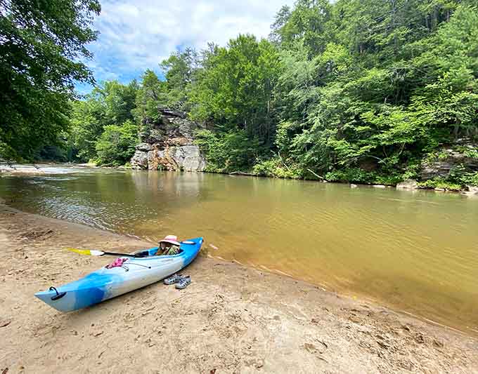 Your kayak rests on golden sand while ancient rock formations stand guard over this peaceful riverside sanctuary.