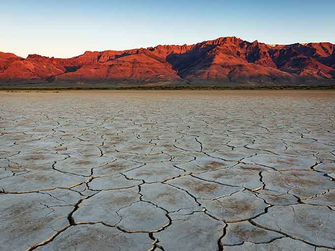 Sunset paints the mountains crimson while the dry lakebed reflects the fading light like ancient pottery.