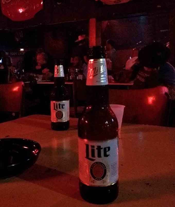 Cold bottles catching crimson light while patrons gather in the shadows, perfectly normal Friday night stuff.