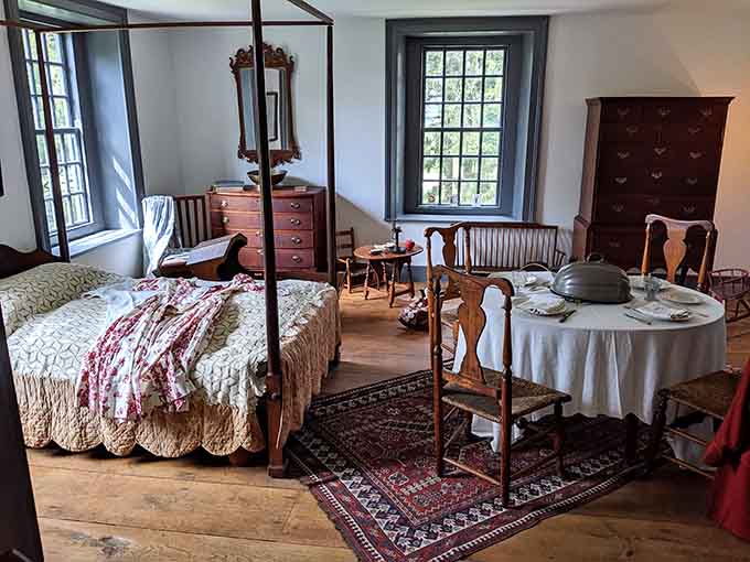 This bedroom looks like someone just stepped out, quilt tossed aside, dinner table waiting. Colonial life, paused perfectly.