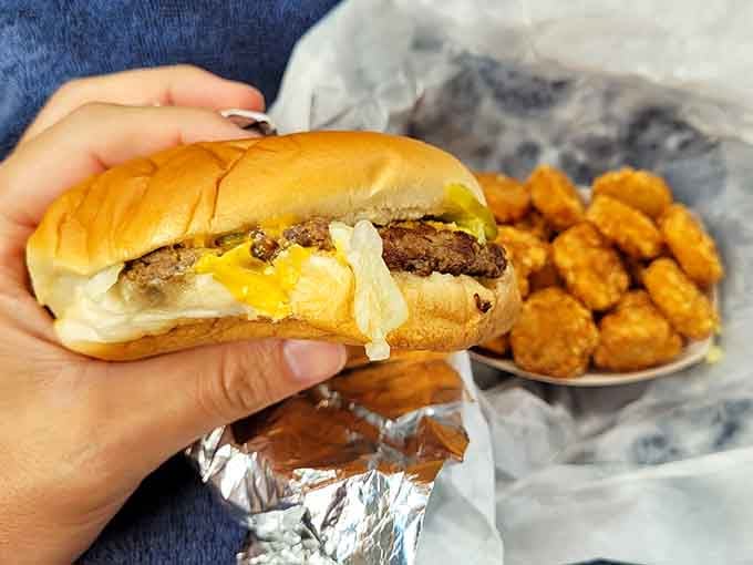 Behold the cheeseburger in its natural habitat: nestled in foil, accompanied by golden tater tots, living its absolute best life.