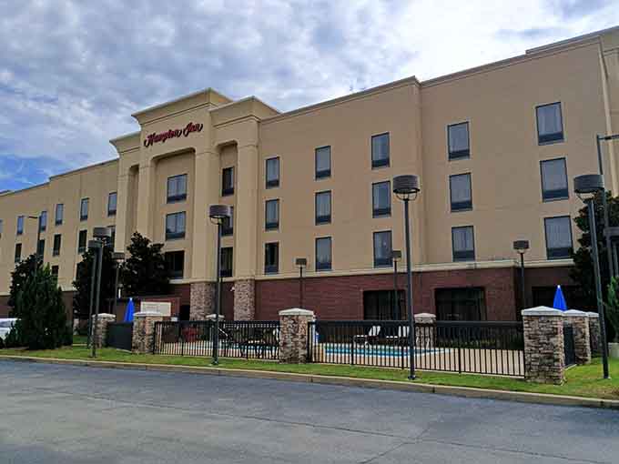 The Hampton Inn Gadsden stands tall against a cloudy Alabama sky, with a poolside fence that practically whispers, "You've earned this."