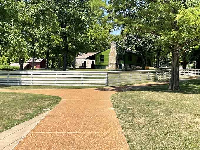 A curving terracotta path leads you toward history, white fences, and a green house that absolutely refuses to be ignored.