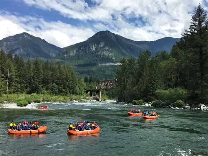 Orange rafts navigate the Skykomish's emerald waters while dramatic peaks stand guard like nature's own security detail.