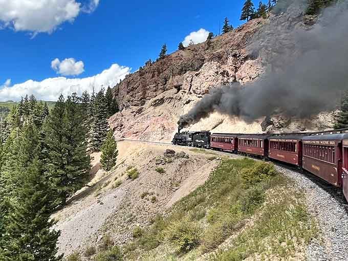 Dark red cars curving through rocky high-country terrain with smoke trailing behind &mdash; the Cumbres & Toltec means serious business up here.