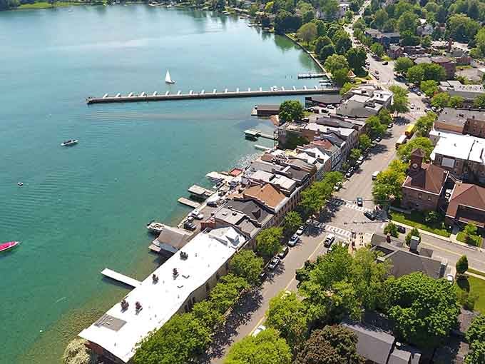 A lone sailboat drifting across jewel-blue water beside a charming waterfront village — honestly, who needs St. Barts?