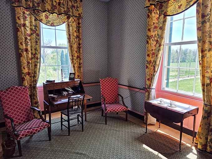 Floral drapes, red upholstered chairs, and sunlight pouring across the grounds make this sitting room feel surprisingly alive.