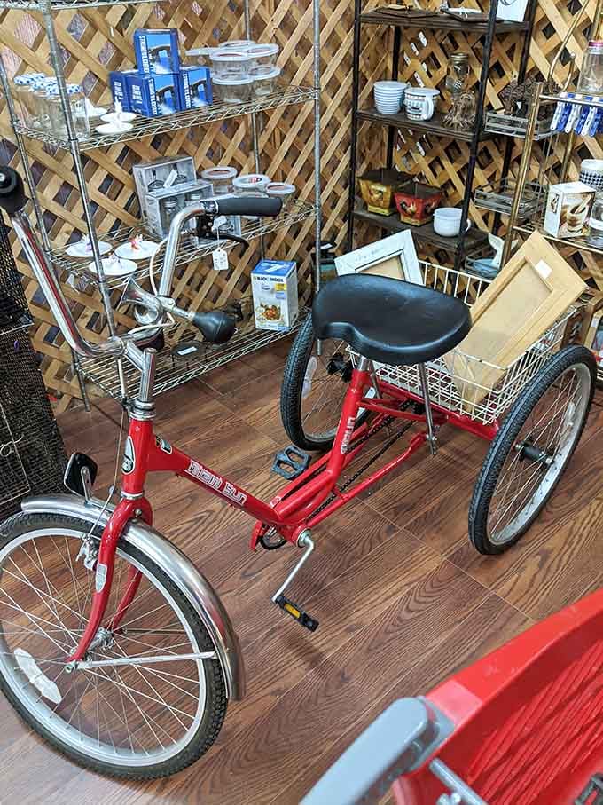 A bright red adult tricycle sitting among shelves of goods, because why not ride home in style.