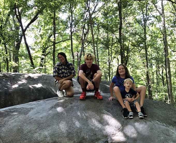 Four happy visitors perched atop a smooth granite boulder, grinning like they just discovered the world's best secret.