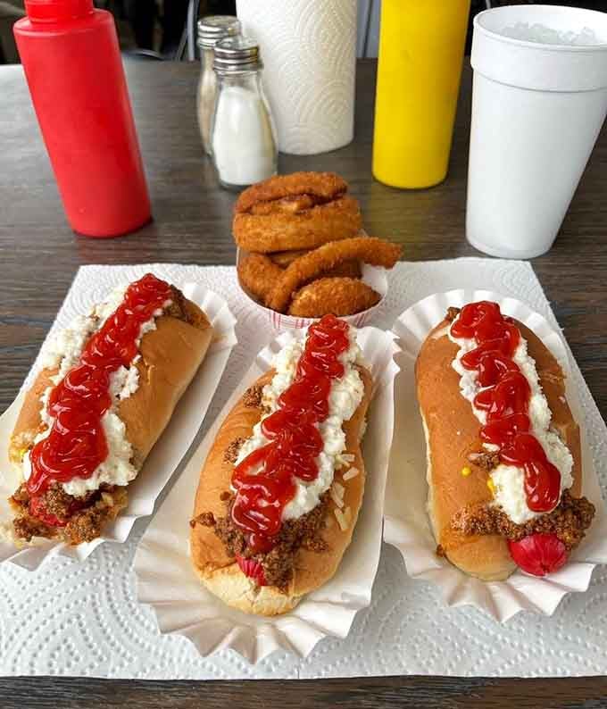 Three slaw dogs lined up like a very delicious reason to cancel your afternoon plans. Those onion rings aren't helping your willpower either.