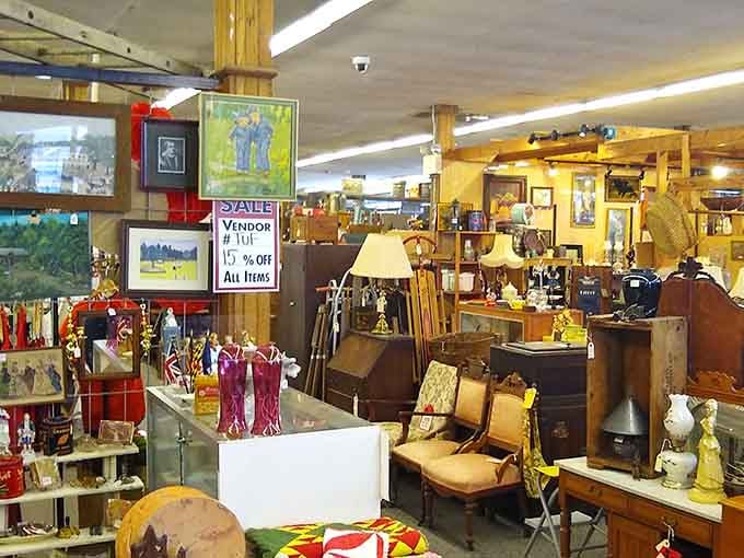 Browse through a charming booth packed with framed artwork, wooden chairs, vintage lamps, and tempting vendor discount signs.