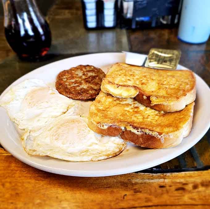 Two eggs, a sausage patty, and Texas French toast stacked together like old friends on a plate.