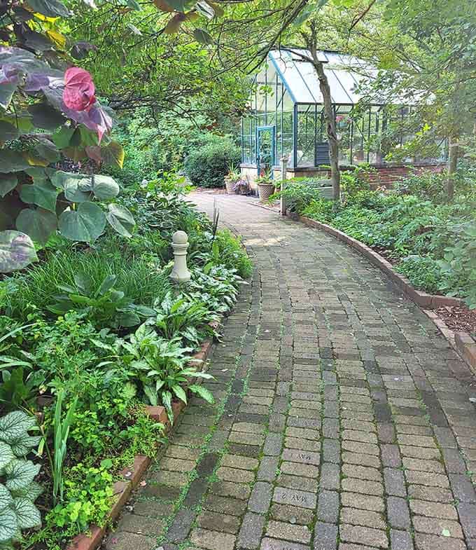 A brick path curving toward a glass greenhouse is basically nature's way of saying "keep walking."