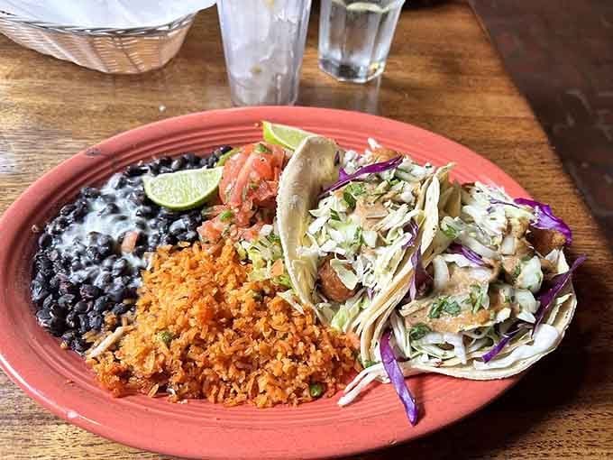 Two fish tacos, black beans, and rice on a terracotta plate, simple, honest, and completely irresistible.