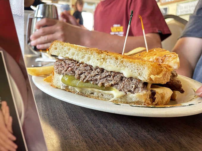 The Brian Burger, grilled to perfection on toasted bread, with pickles peeking out like they earned it.