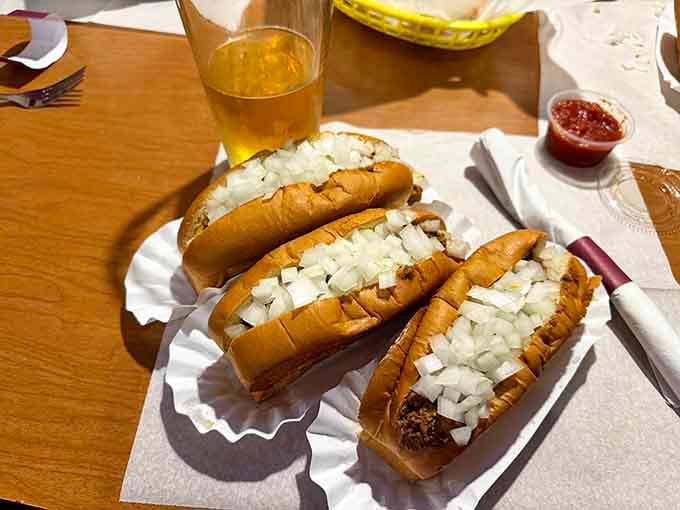 Three plain Coneys lined up like edible soldiers, their chopped onions glistening like tiny flavor diamonds on parade.