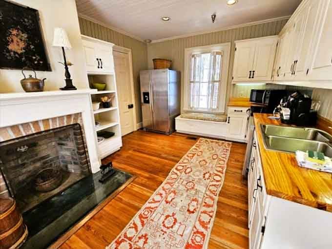 A kitchen with a fireplace and hardwood floors proves that historic charm and a modern fridge can absolutely coexist peacefully.