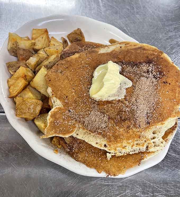 Buttermilk pancakes dusted with cinnamon sugar and topped with butter, spilling off the plate like they simply ran out of room.