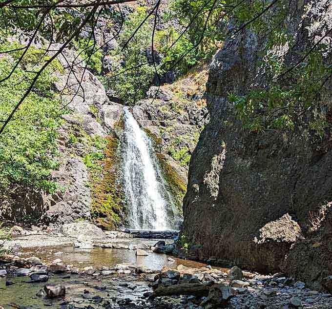 Sunlight catches the spray as water plunges between dark stone walls into a pool framed by ancient rocks.
