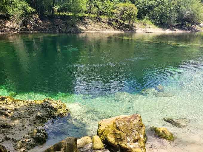 Moss-covered rocks at the water's edge, a sandy natural shoreline, and that impossibly clear green water quietly daring you to jump in.