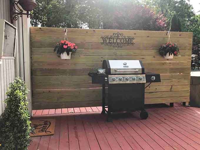 A gas grill, hanging flowers, and a "Welcome" sign on a wooden wall, this deck means business.
