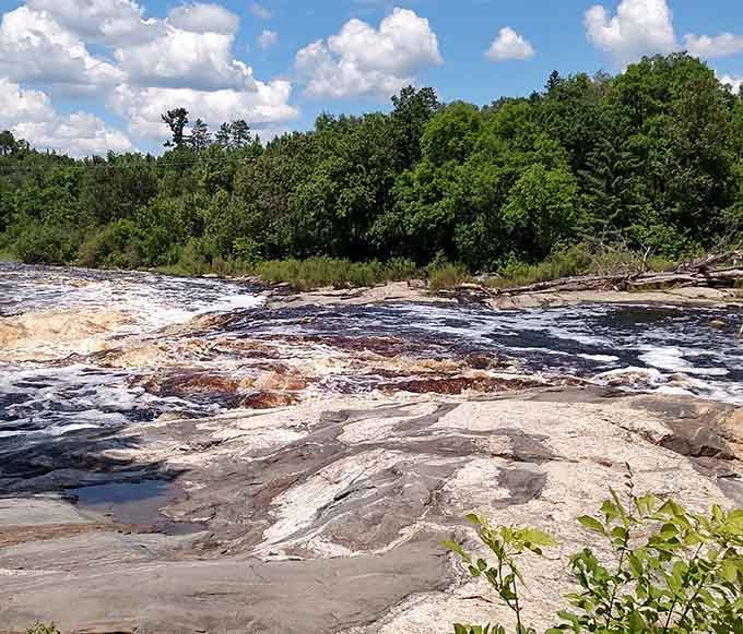 Fluffy white clouds drift over the lush green forest as the river continues its steady journey through the rocky landscape.