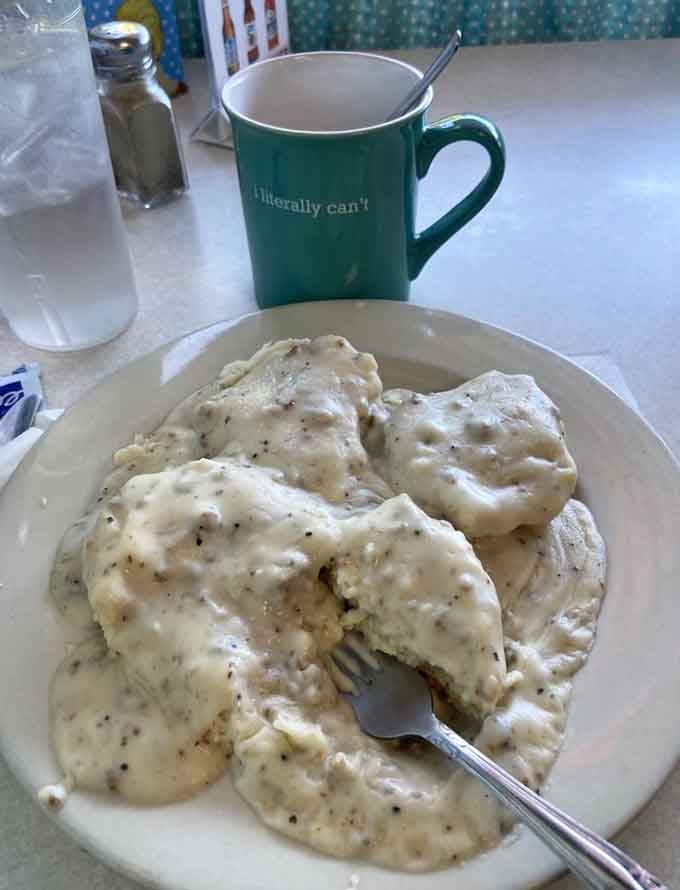 Two biscuits buried under scratch-made sausage gravy, and a coffee mug that speaks for all of us.