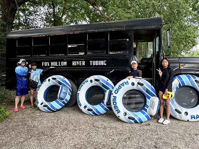 Happy tubers pose with their Rapid Rider tubes beside the iconic black Fox Hollow bus, ready for the river.