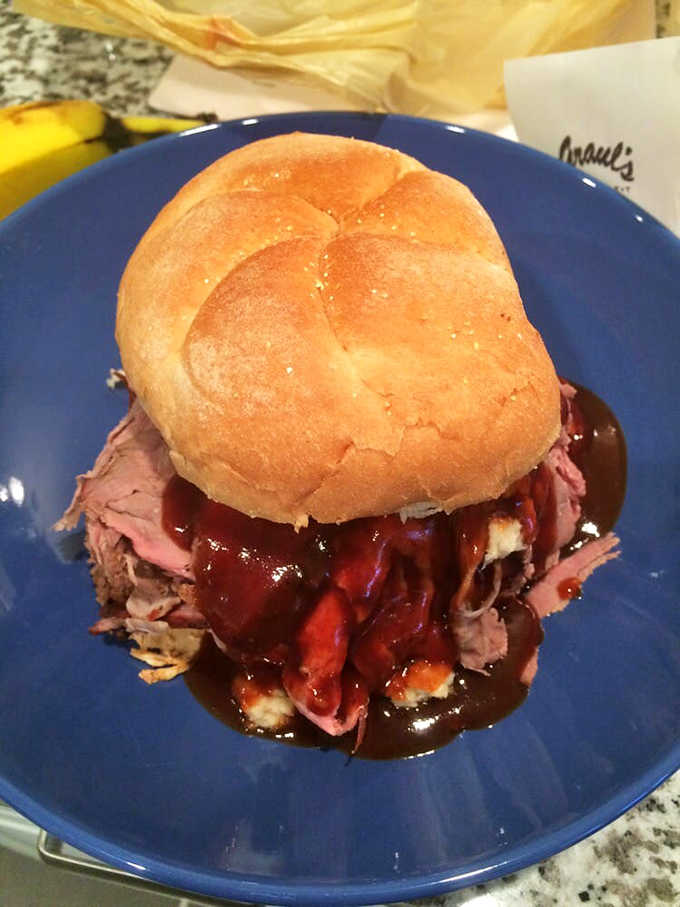 Smoked beef piled onto a bun with BBQ sauce pooling around it like a delicious moat.