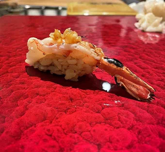That shrimp nigiri on a lacquered red board looks like it was placed there by someone who takes beauty as seriously as flavor.
