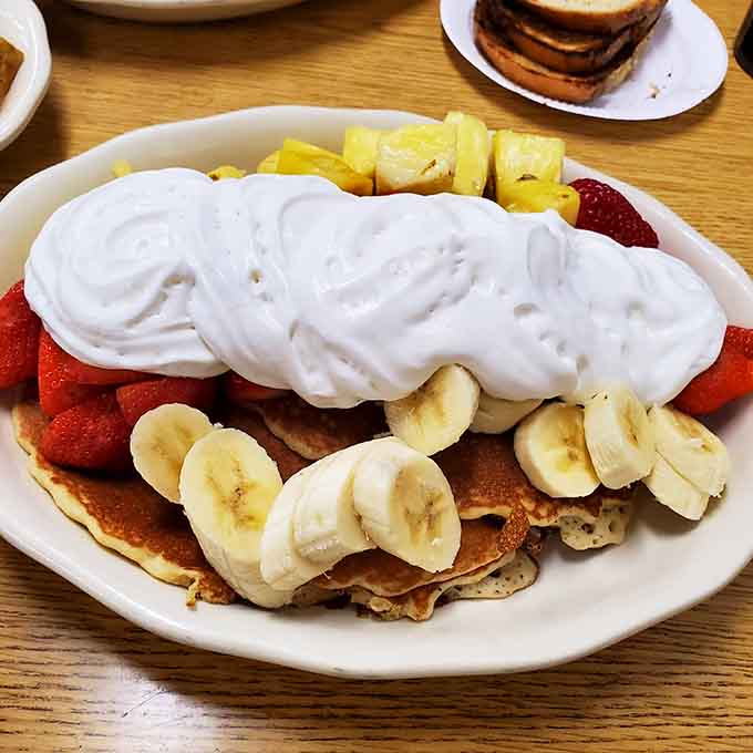 Buttermilk cakes buried under strawberries, bananas, pineapple, and a mountain of whipped cream. Breakfast called, it wants to be a party.