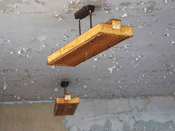 Rust-covered light fixtures hang from a crumbling ceiling like forgotten punctuation marks at the end of a very long sentence.