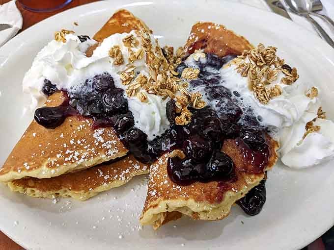 Blueberries, whipped cream, and granola piled high on golden pancakes, breakfast just called and it wants a standing ovation.