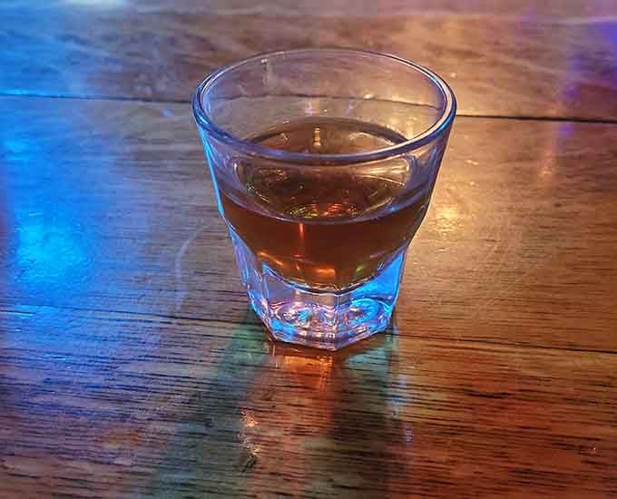 A shot of something amber and serious, sitting on a wooden bar that has seen more history than most textbooks.
