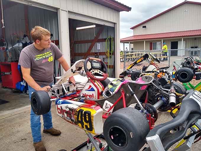 A young fan in a Jimmie Johnson shirt inspects a BirelART kart with the focused intensity of a seasoned pit crew chief.