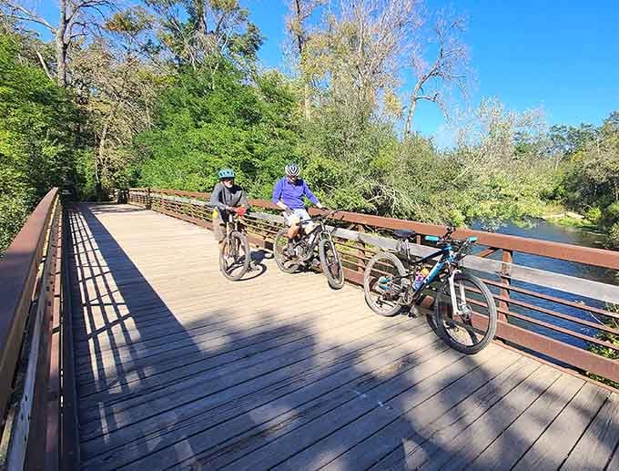 Two cyclists pause on a sun-drenched bridge over the Willow River, proving that the best conversations happen when you stop pedaling.