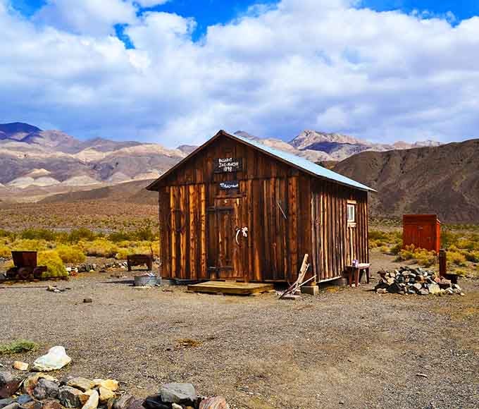 One lone wooden cabin standing against a sky full of drama, surrounded by nothing but desert silence.