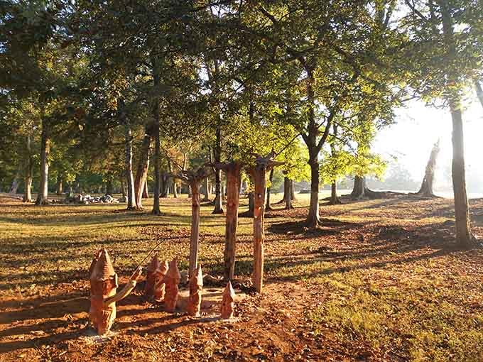 Golden afternoon light filters through the trees, illuminating carved wooden faces that seem to watch over the park.