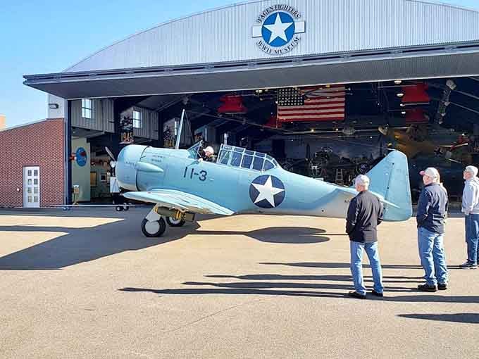 A beautifully restored WWII trainer aircraft rolls out of the hangar under a wide blue sky, looking ready for duty.