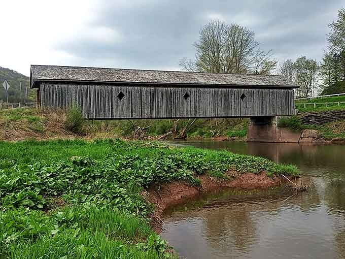 Three diamond windows cut into weathered gray wood, a muddy creek below — this bridge has seen every season and survived them all.