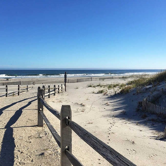 Weathered wooden fences guide you through soft dunes toward crashing waves, like a gentle nudge from the shore itself.