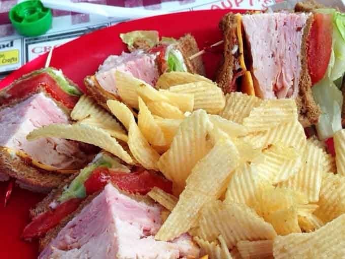 A club sandwich stacked thick with ham, turkey, tomato, and lettuce, with a mountain of ridged chips alongside. Lunch goals, achieved.
