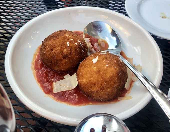 Two perfectly golden arancini sitting in a pool of sauce, topped with shaved cheese. Crispy outside, deeply satisfying inside, gone embarrassingly fast.