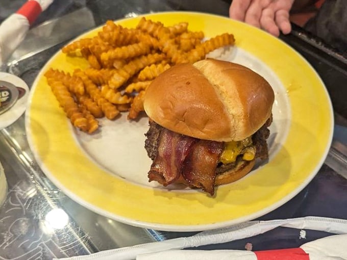 A smash burger stacked with bacon and melted cheese, sitting next to a pile of crinkle-cut fries. Pure, unapologetic comfort food.