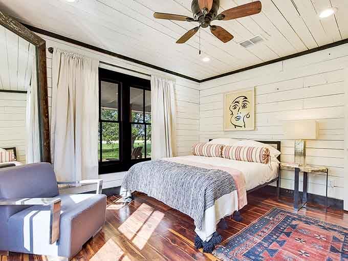 Sunlight pouring through black-framed doors, a cozy bed, and original artwork on the wall. Sleeping here feels like staying in a gallery.