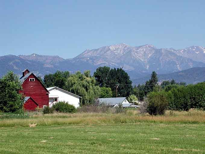 A classic red barn, a white farmhouse, and the Wallowa Mountains rising behind them like nature's own backdrop curtain.