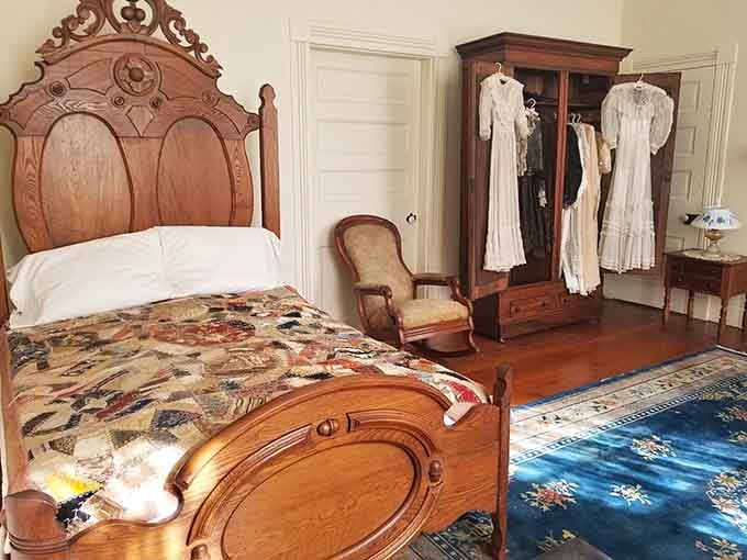 An ornate oak bed and open wardrobe with period dresses, simple furnishings that once held a remarkable life.